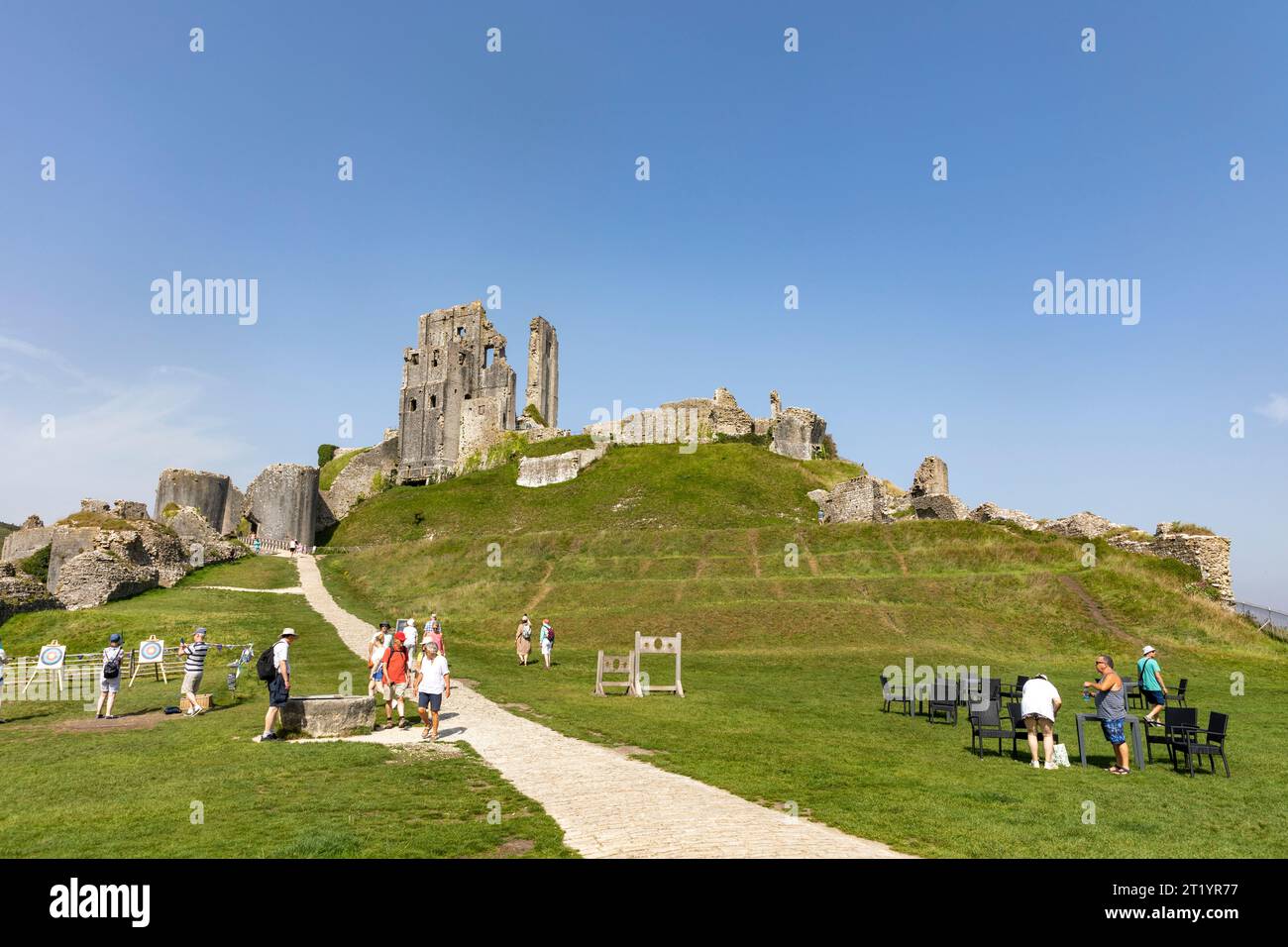 Corfe Castle grounds with seating and tables and visitors using archery ...