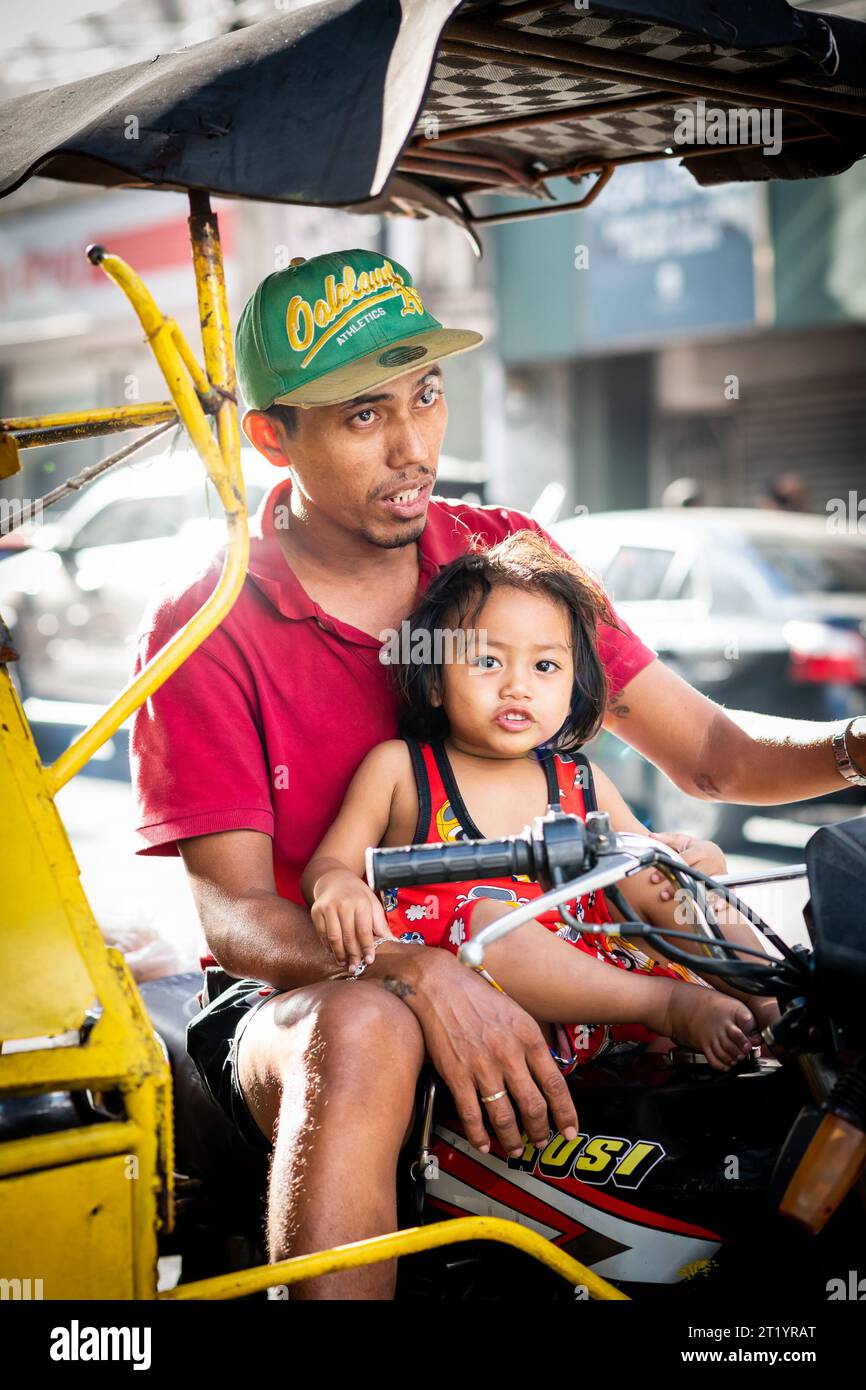 A Filipino father plays with his cute daughter sat on his tricycle ...