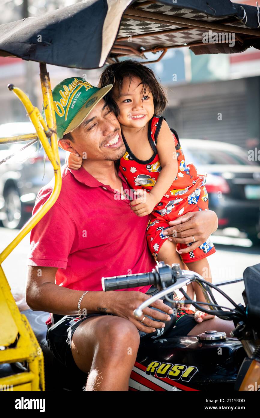A Filipino father plays with his cute daughter sat on his tricycle ...