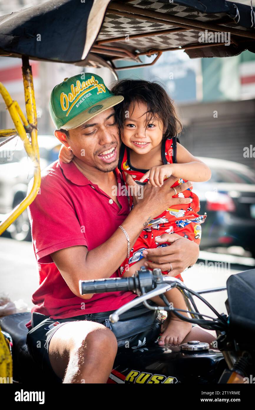A Filipino father plays with his cute daughter sat on his tricycle ...
