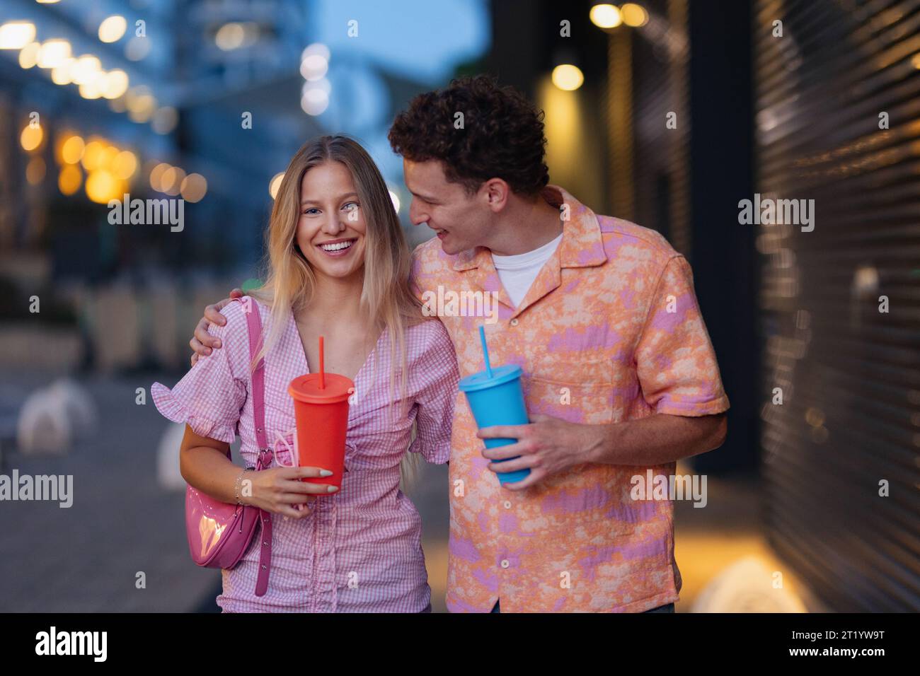 Gen Z couple in pink outfits leaving the cinema with drinks in hand ...