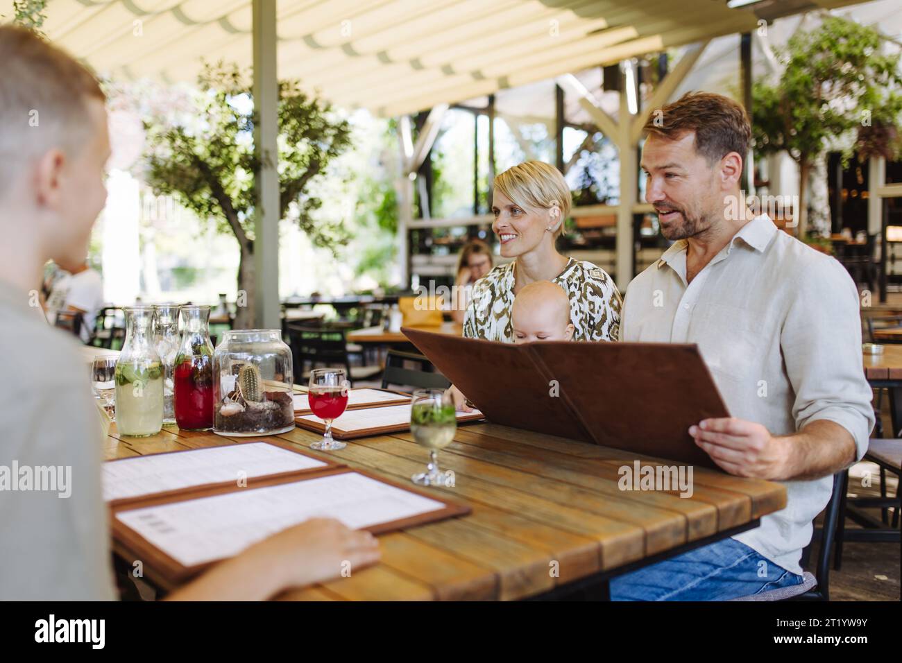 Family with baby and daughter reading menus in a restaurant, choosing ...