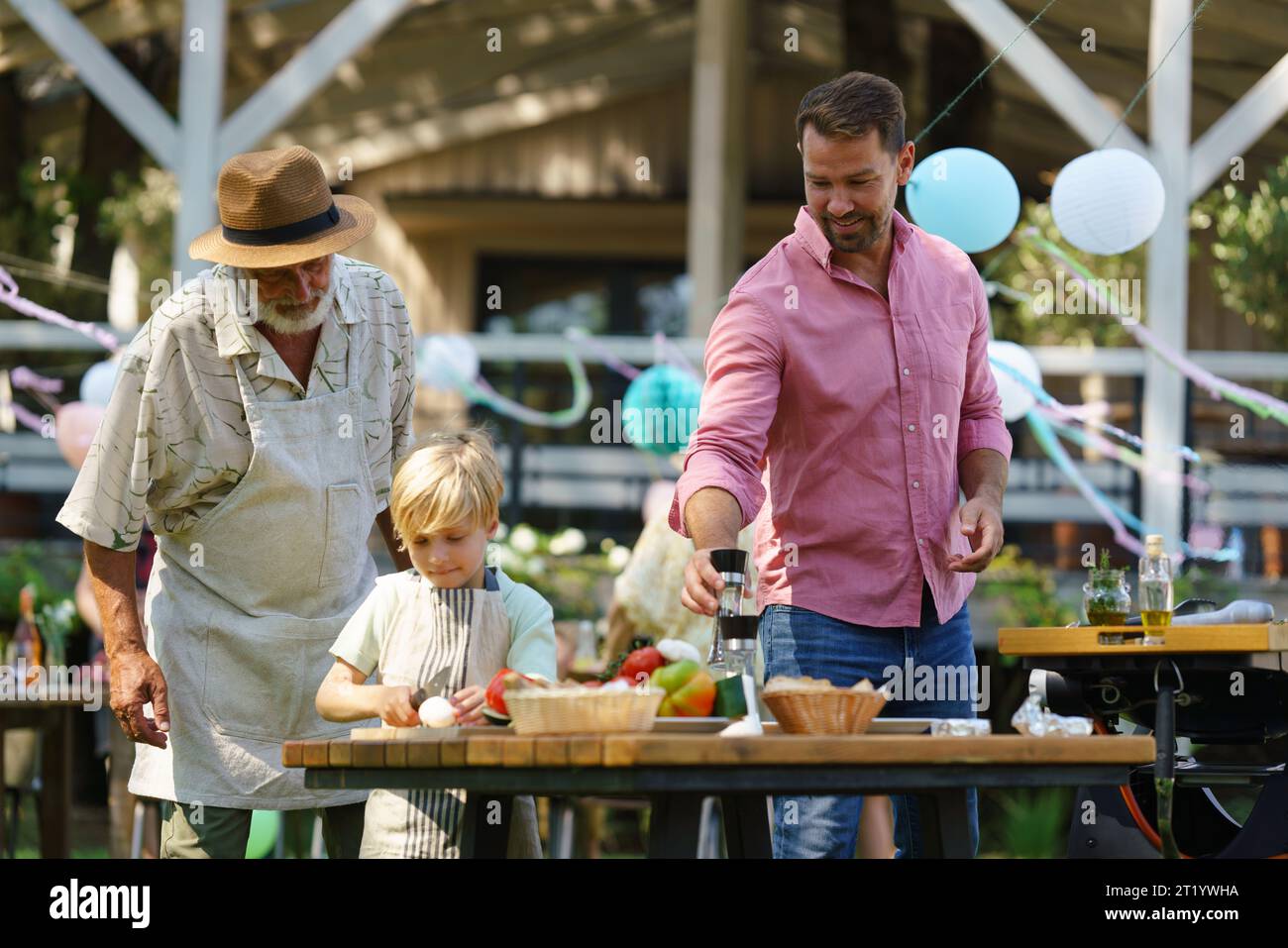 Young boy cutting vegetables for grilling. Father, grandfather and son grilling together at ...