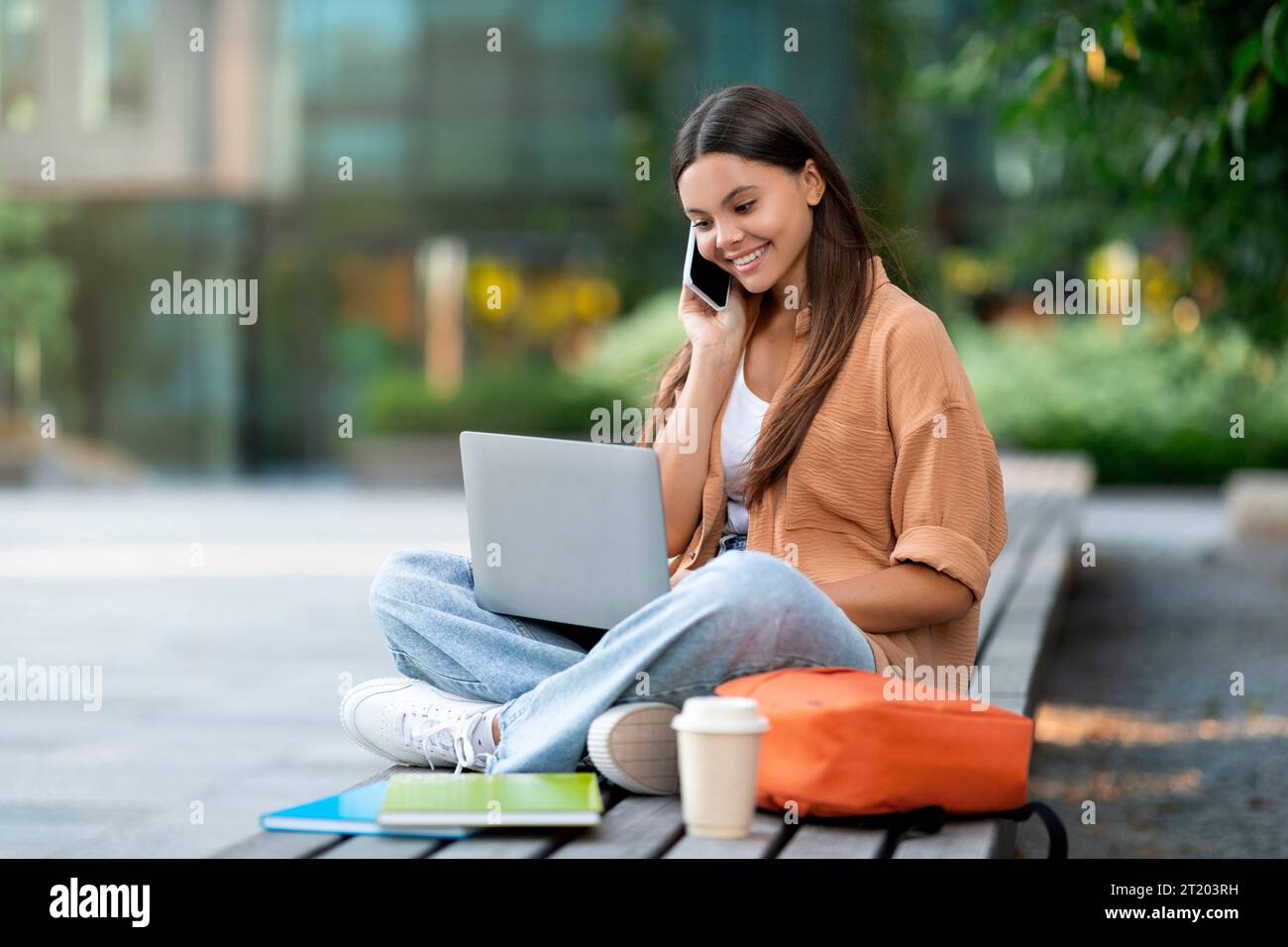 Smiling student talks on phone while using laptop, empty campus Stock ...