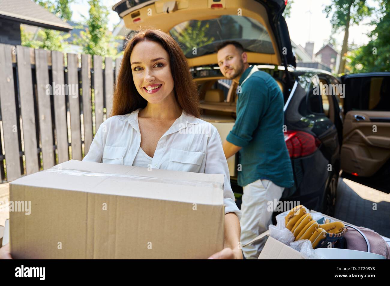 Smiling woman carries a box of things from the trunk Stock Photo - Alamy