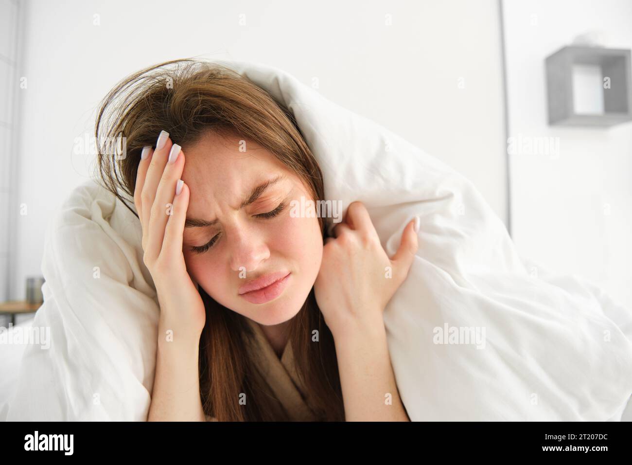 Close up of woman feeling unwell at home, lying in bed under white ...