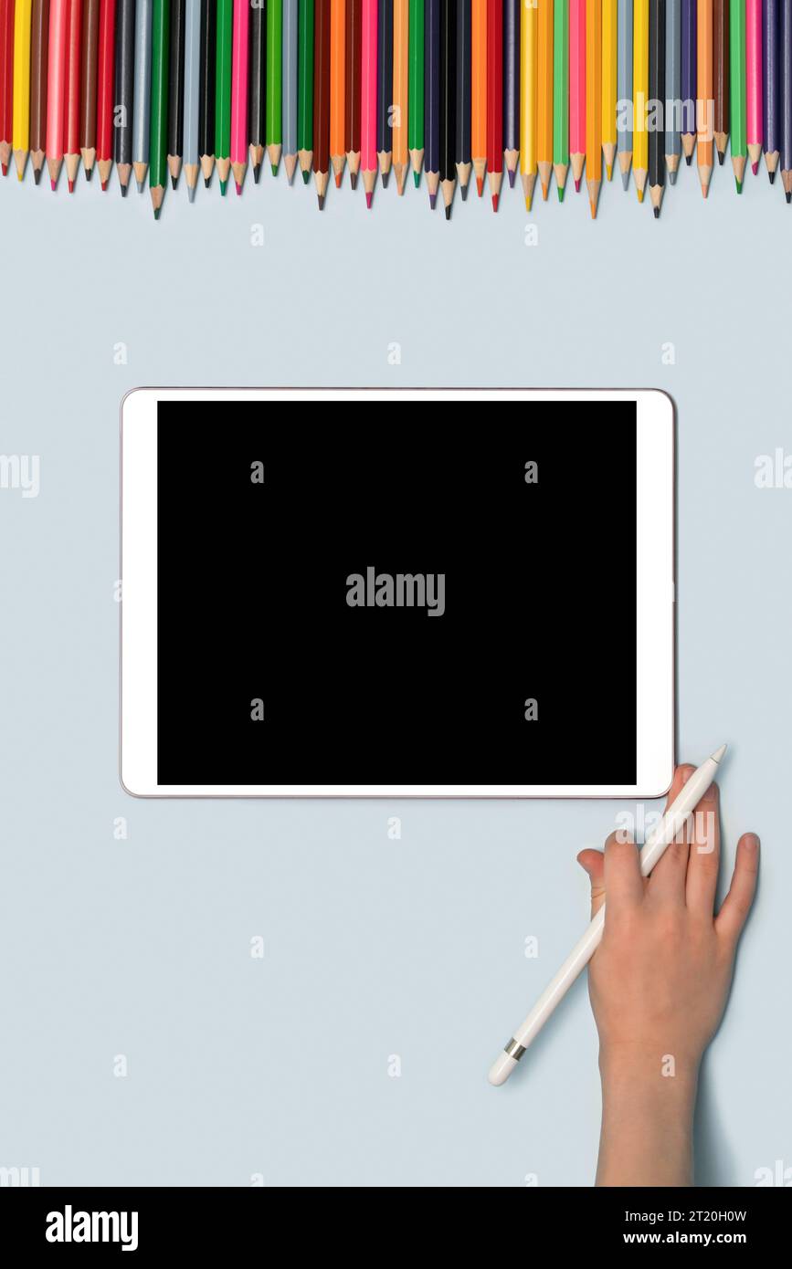 A tablet and a child's hand with a stylus are lying on the table, on ...