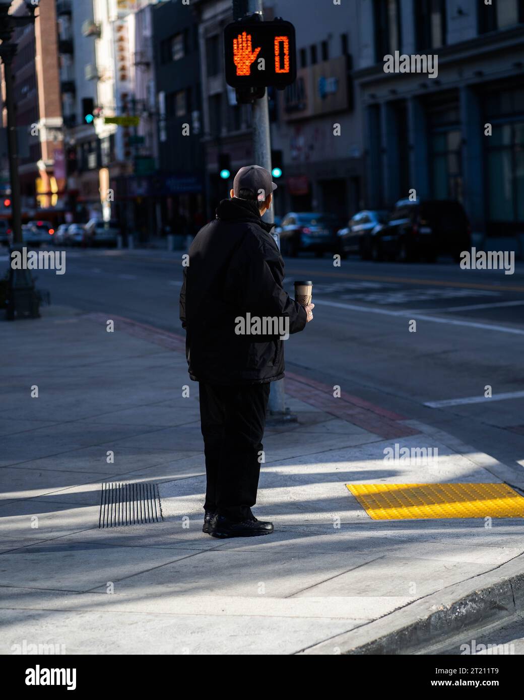 A young man stands on a corner of a busy city street, adjacent to a ...