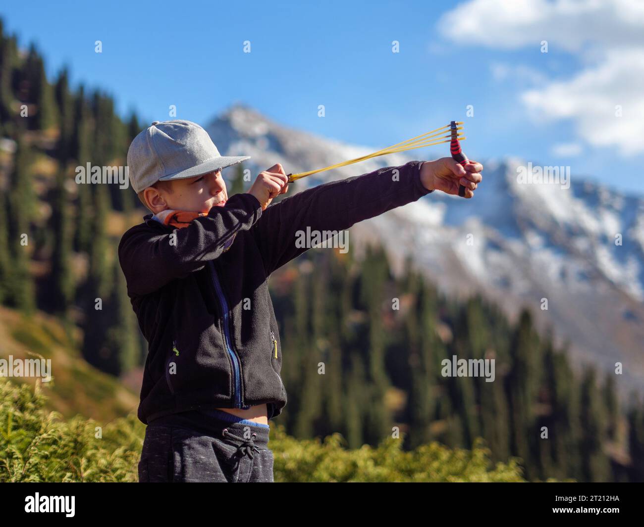 A young boy shoots from a slingshot. Naughty boy having fun outdoors ...