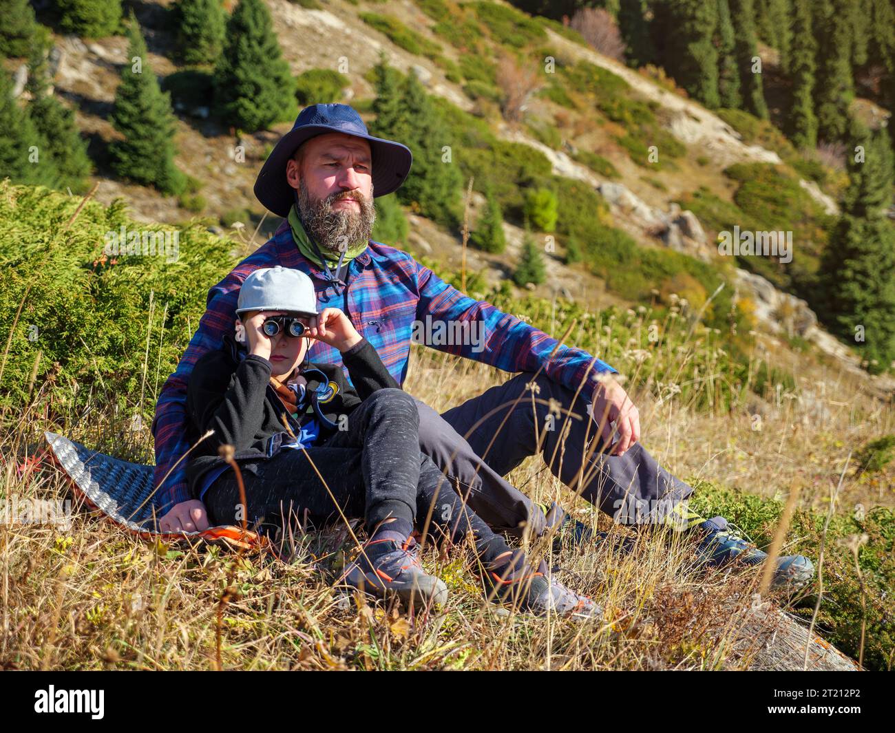 Father and son sit on the mountainside and admire the beautiful view ...