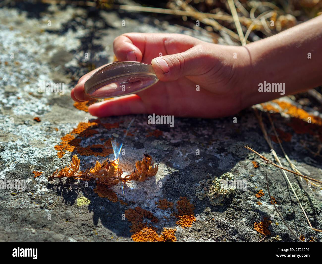 Close-up of a boy's hand making a fire using a magnifying glass ...
