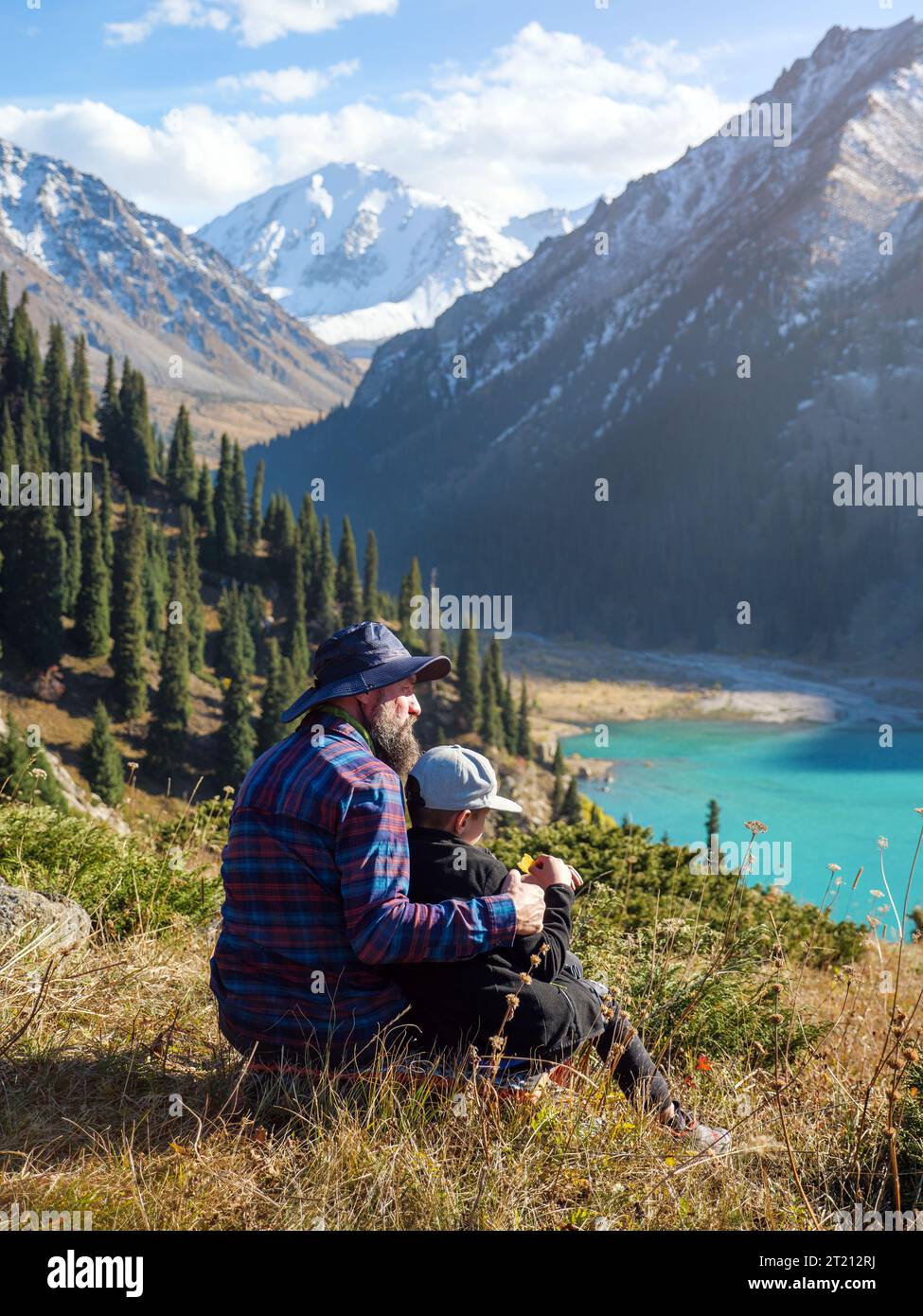 Father and son sit on the mountainside and admire the beautiful view ...