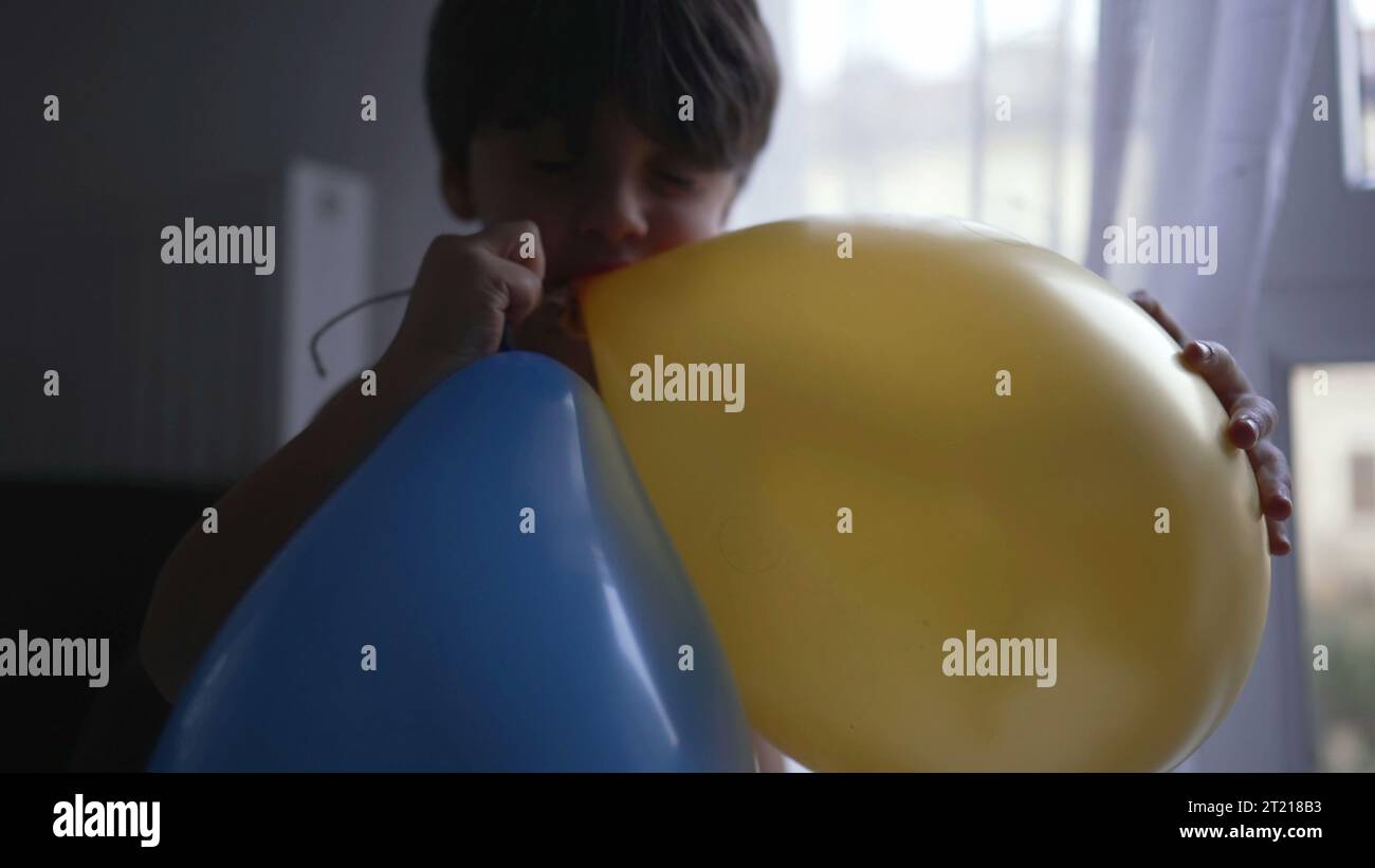 Kid blows up balloons at home after birthday party. Little boy bites ...
