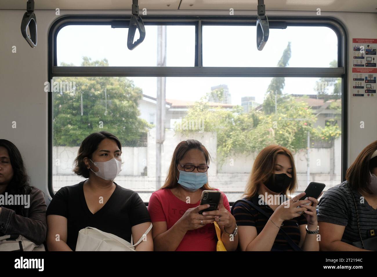 Manila, Philippines: masked female commuters sit on a cabin bench by a ...