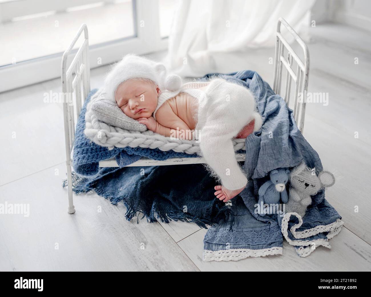 Adorable newborn baby boy sleeping in tiny bed decorated with blankets and knitted toys. Cute ...