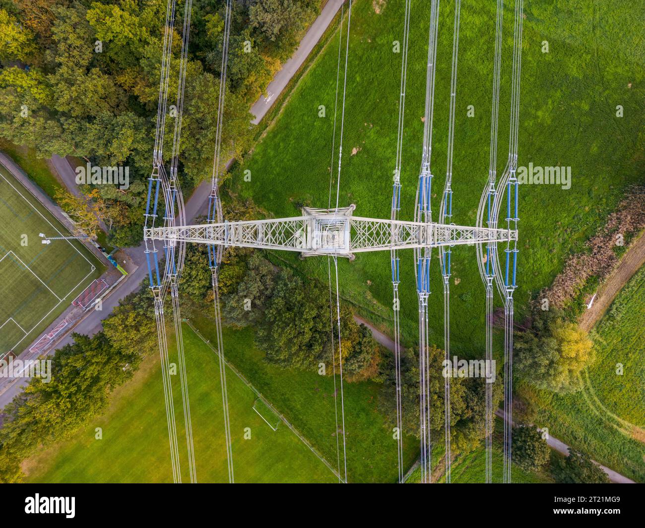High voltage pylon with power lines between nature and sports field ...