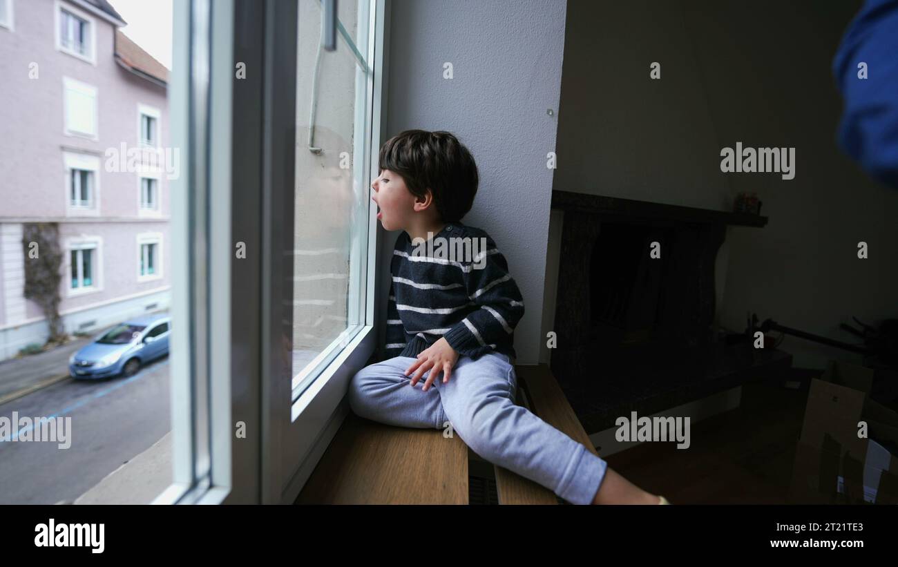 Child's daydream sitting by window at apartment breathing into glass ...