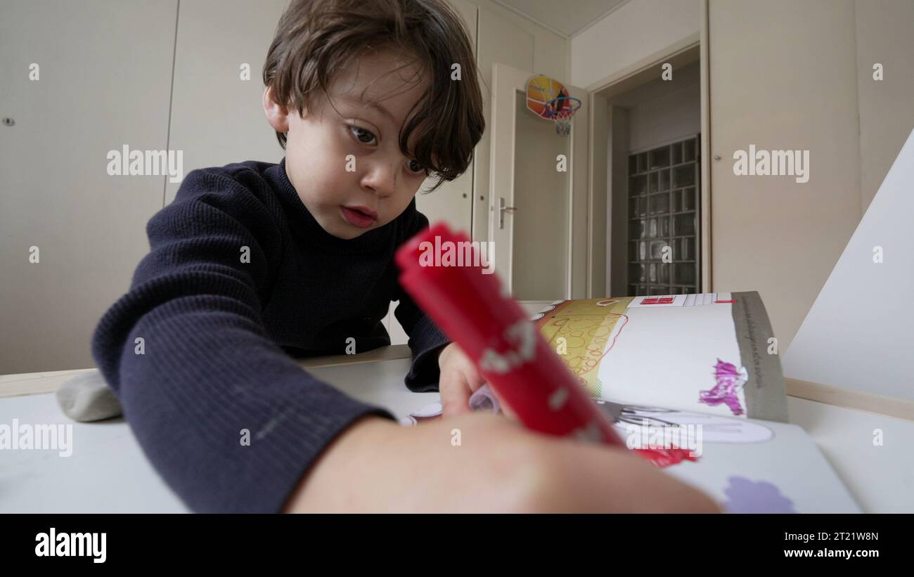 Child holding pen drawing into coloring book with concentrated emotion ...