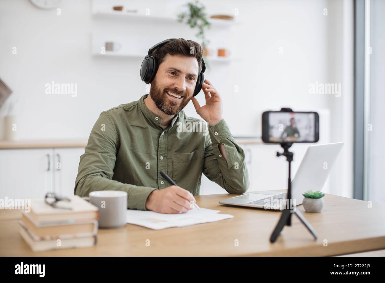 Positive vlogger smiling at mobile camera and making notes Stock Photo ...