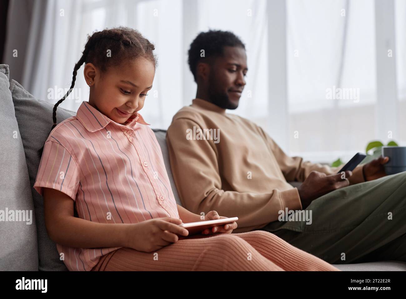 Portrait of cute Black girl using pink tablet or smartphone and playing ...