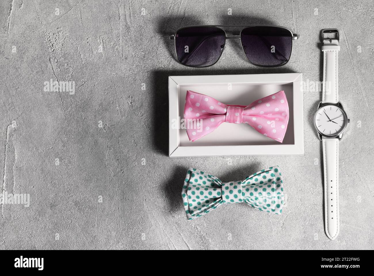 Stylish color bow ties, wristwatch and sunglasses on gray textured ...