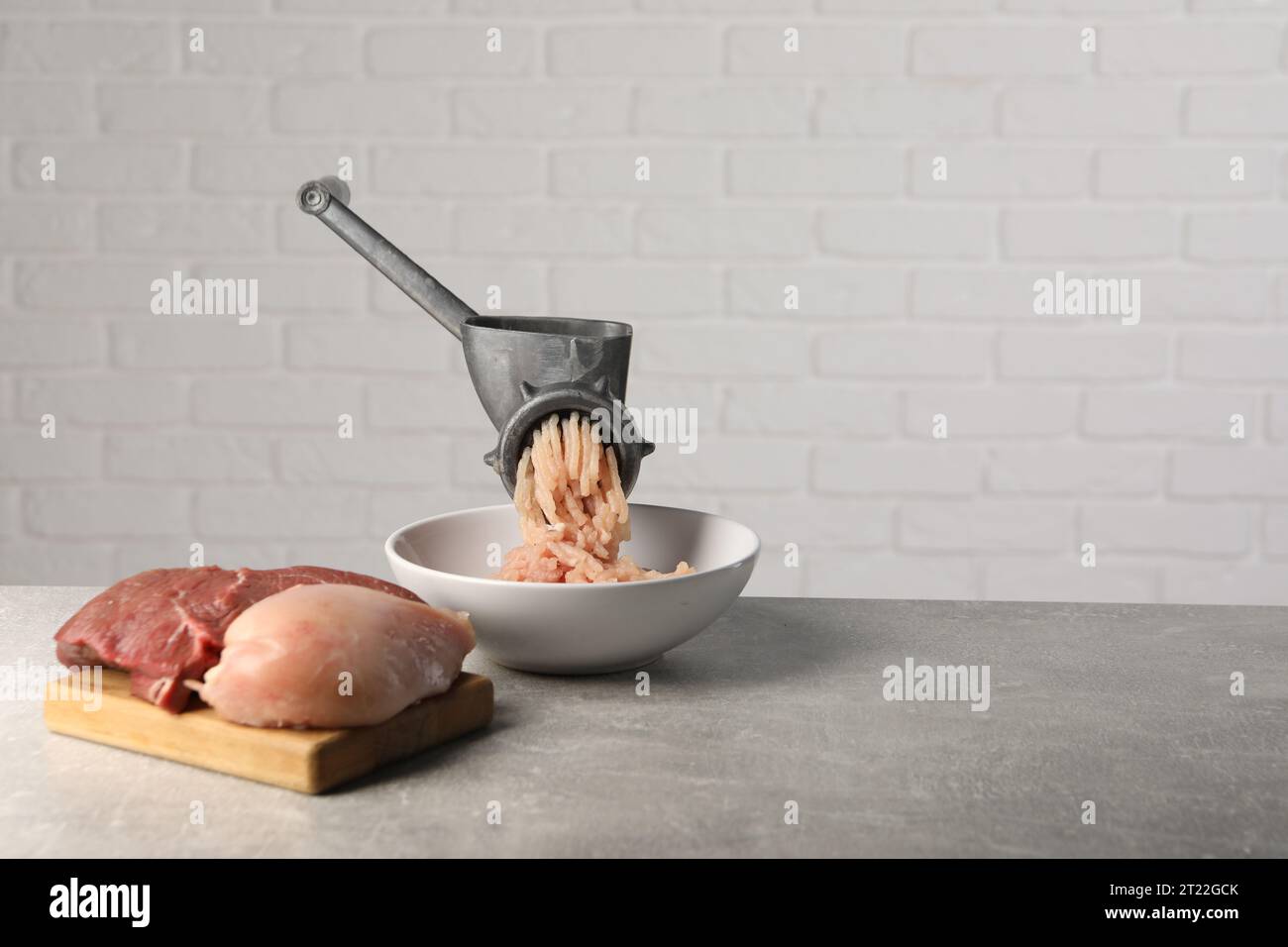 Metal meat grinder with mince, raw chicken and beef on grey table near ...
