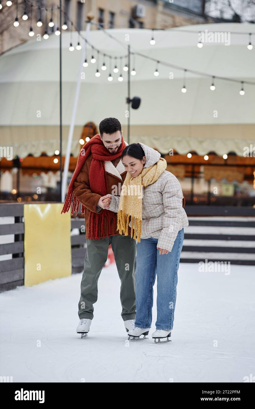 Full length portrait of young couple ice skating together at outdoor ...