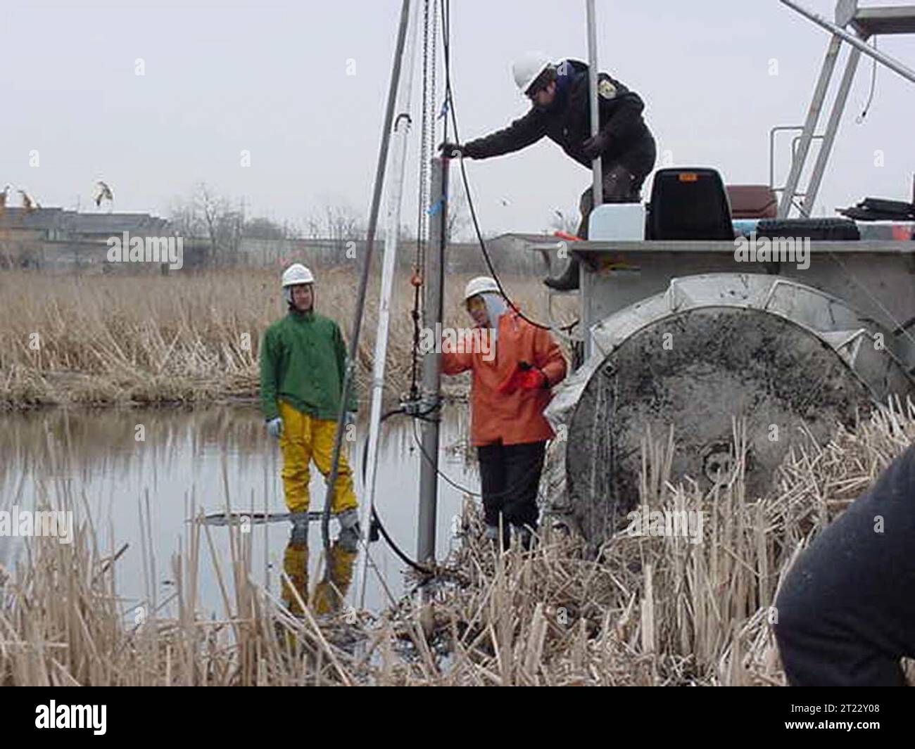 Three workers collect sediment core samples at Roxanna Marsh along the ...