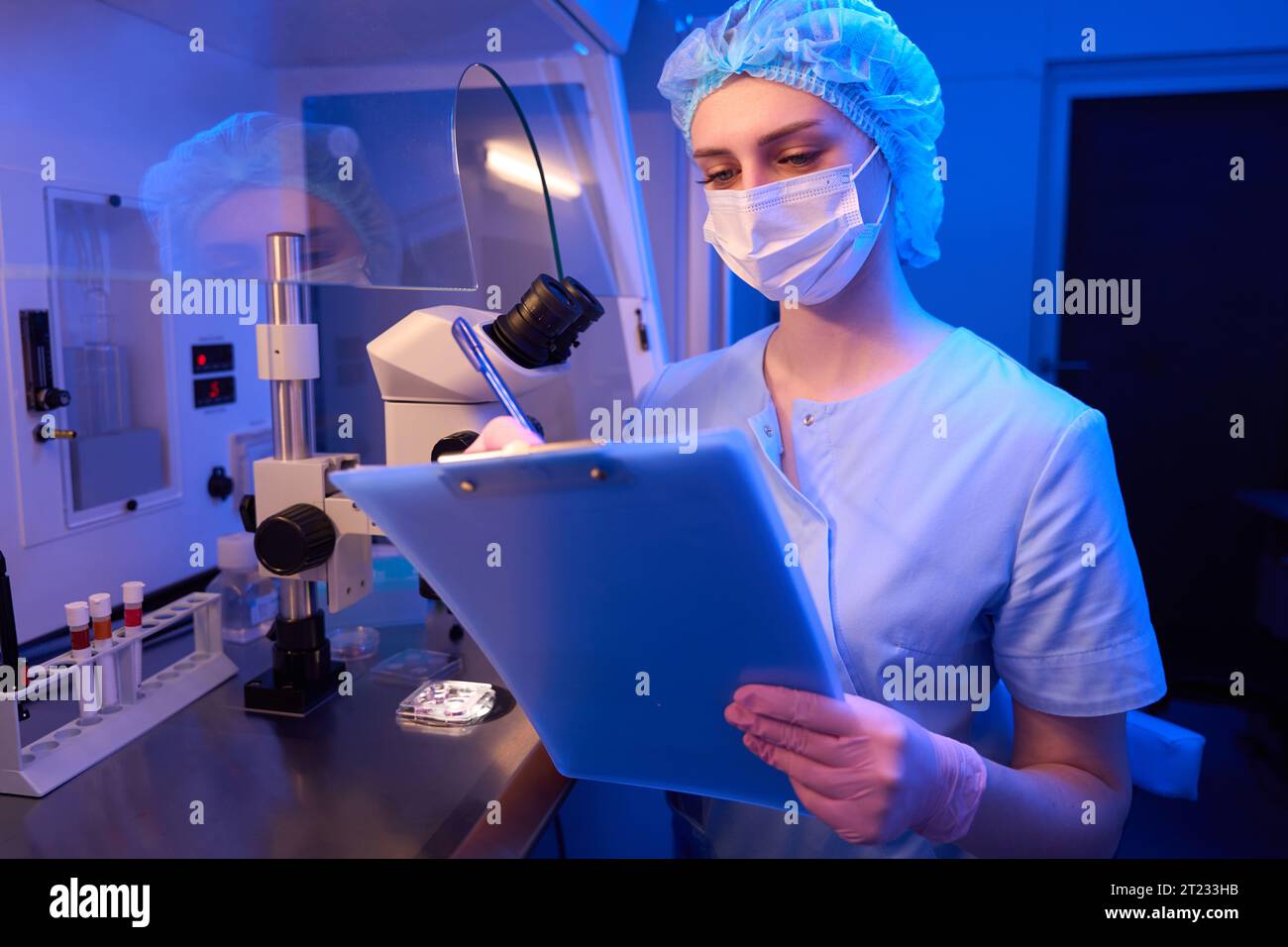 Female scientist taking notes after microscopic examination of cell ...