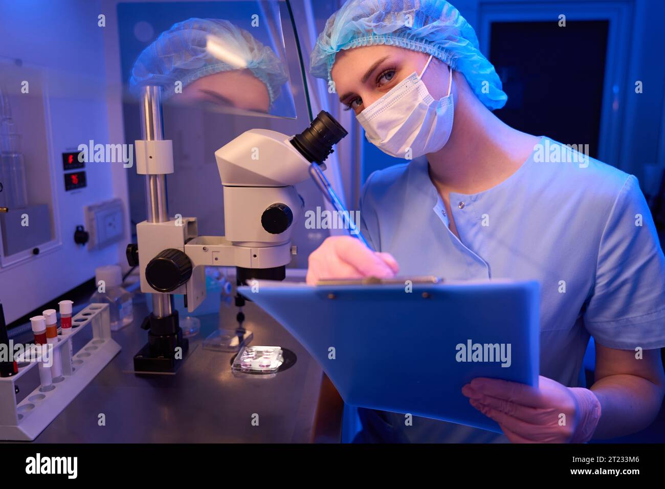 Lab researcher recording results during microscopic examination of cell ...