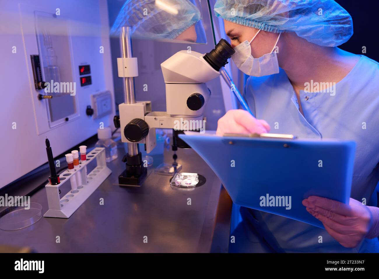 Female scientist taking notes during microscopic examination of cell ...