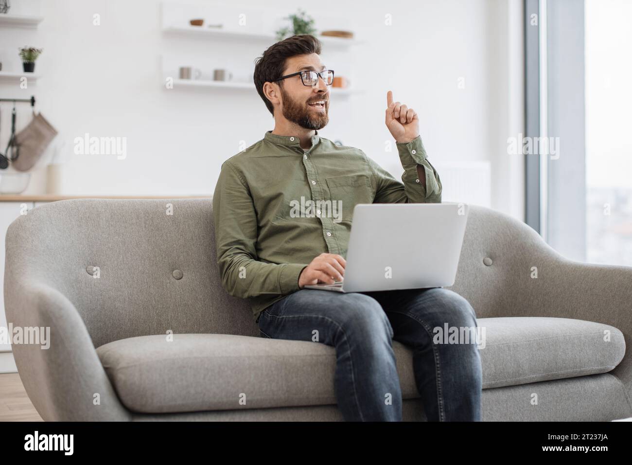 Happy bearded man pointing finger up while sitting on comfy couch and ...