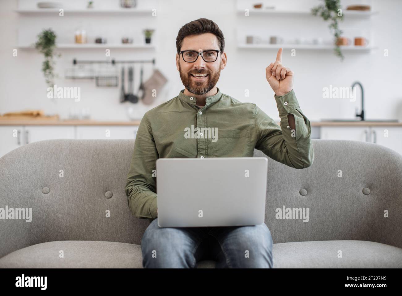 Happy bearded man pointing finger up while sitting on comfy couch and ...