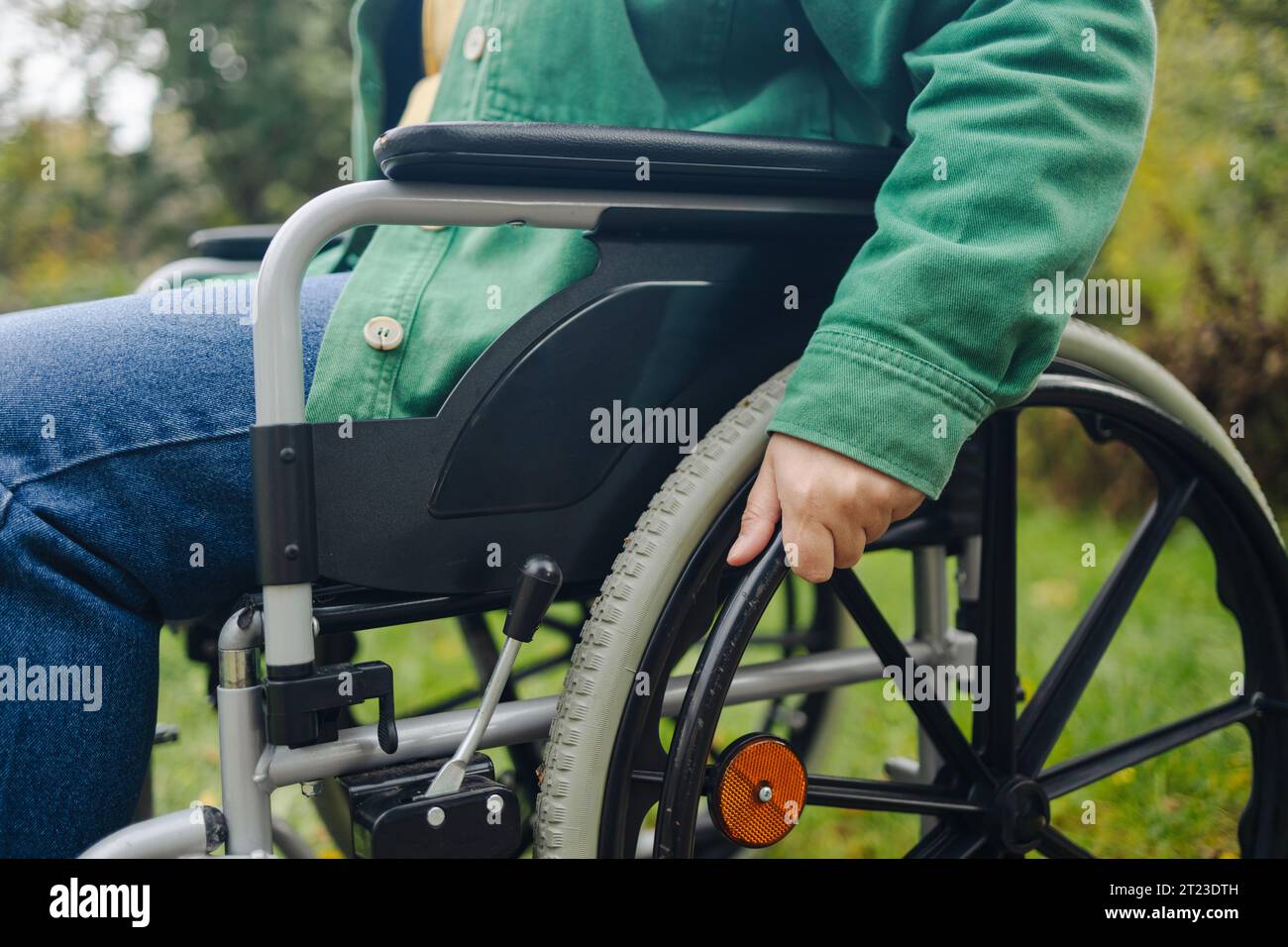 Close-up of female hand on wheel of wheelchair during walk in park ...