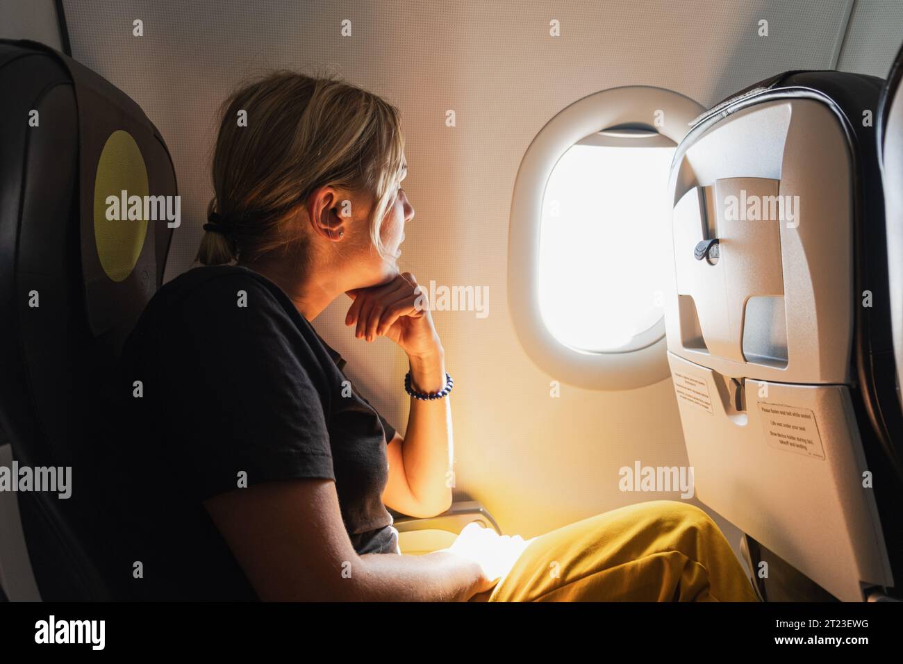 Passenger woman is flying in plane. Girl sitting in airplane looking ...