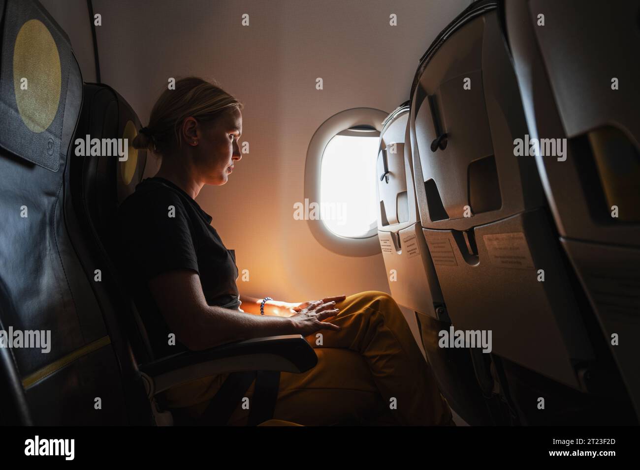 Passenger woman is flying in plane. Girl sitting in airplane looking ...