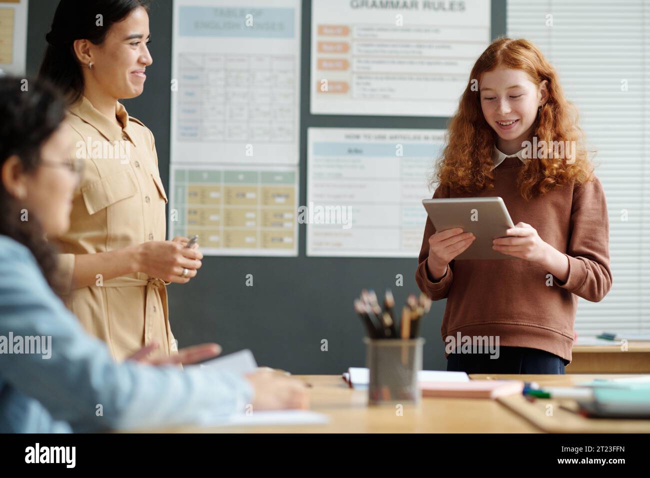 Clever smiling schoolgirl looking at tablet screen during presentation ...