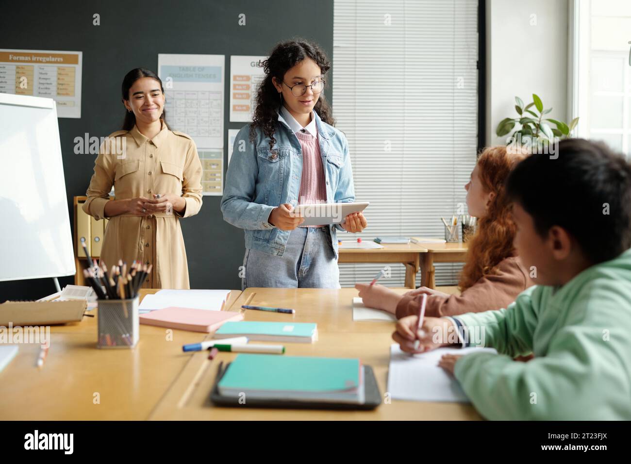 Confident schoolgirl in casualwear standing in front of classmates ...