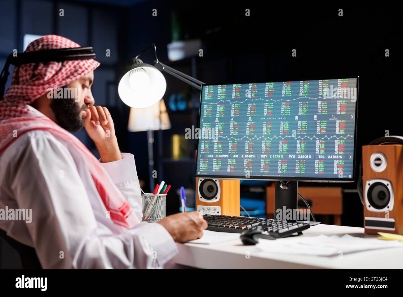 Middle Eastern man seated on his desk carefully researching and jotting ...