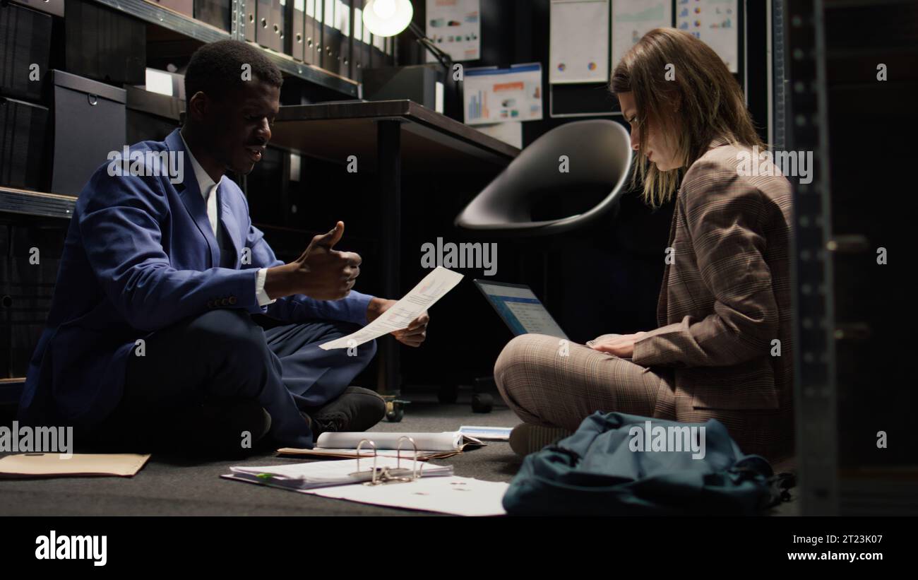 Male inspector and female police officer seated on office floor with ...