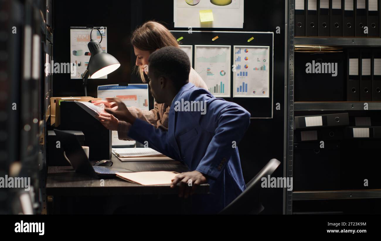 Interracial police partners conduct detective work, examining evidence ...