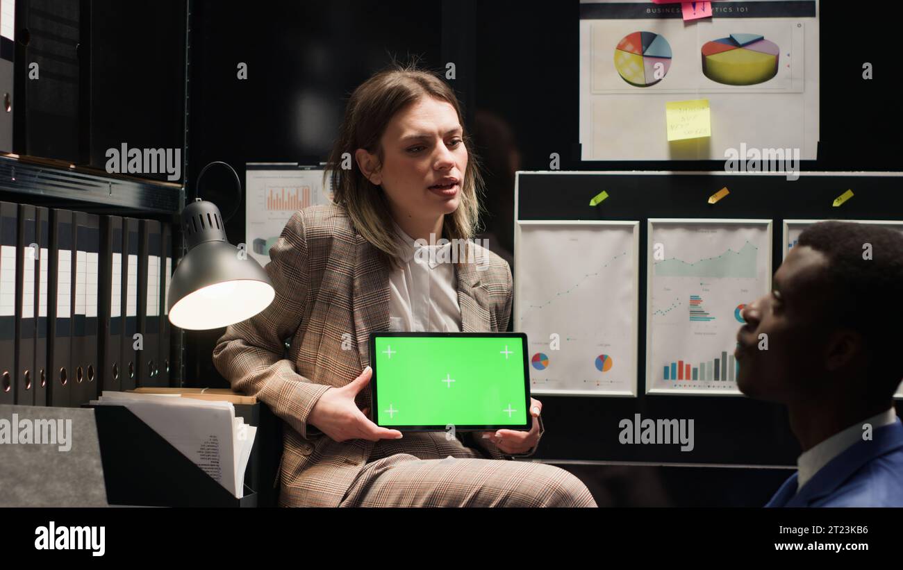Caucasian private detective holds tablet with greenscreen, as black ...