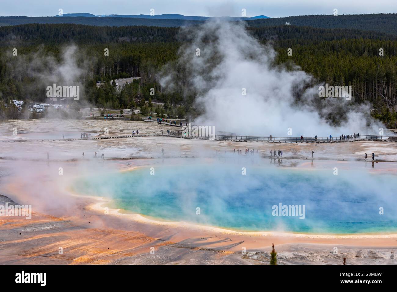 Tourists walk along boardwalk and view colorful blue pool of grand ...