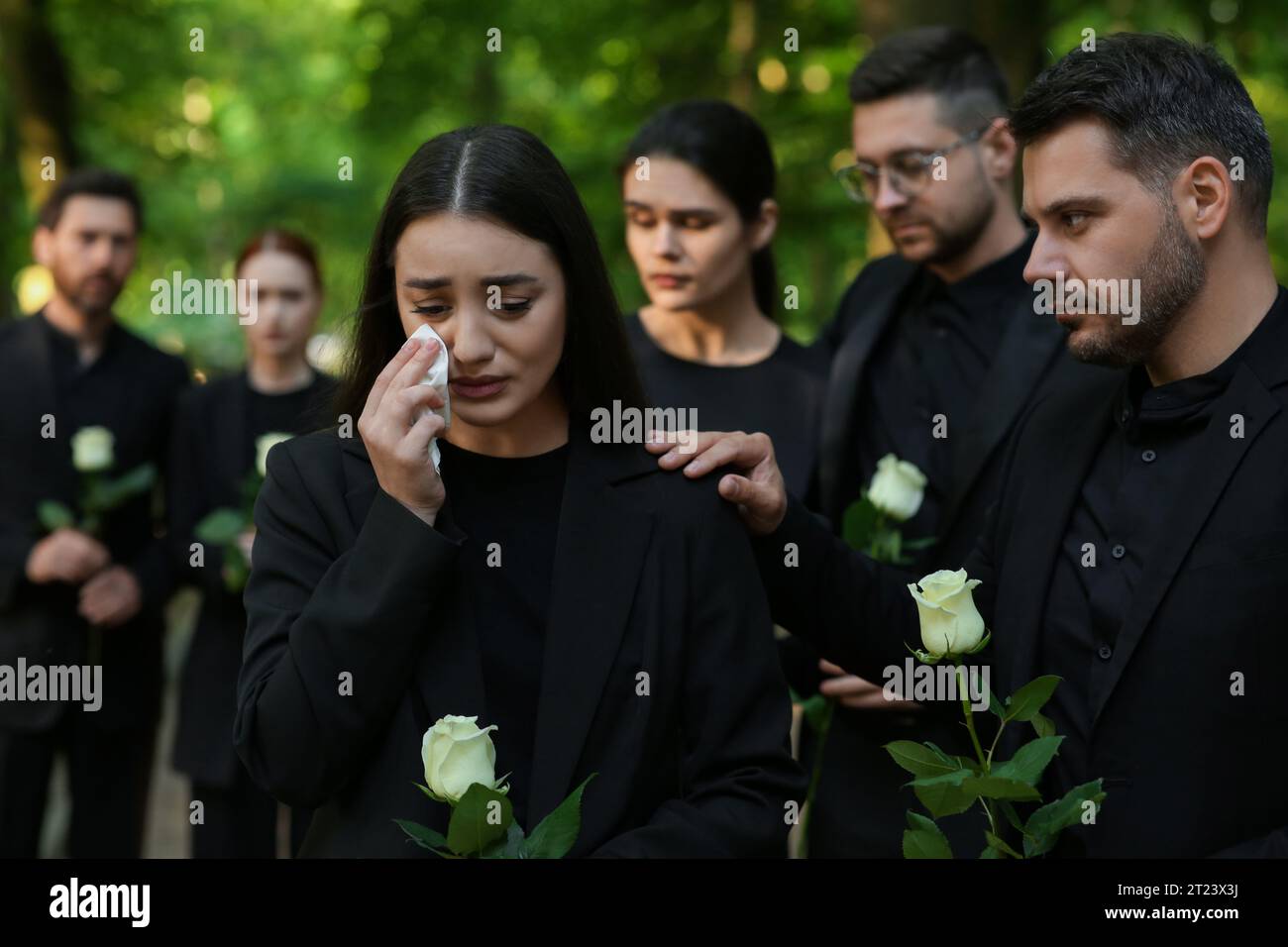 Funeral ceremony. Sad people with white rose flowers mourning outdoors ...