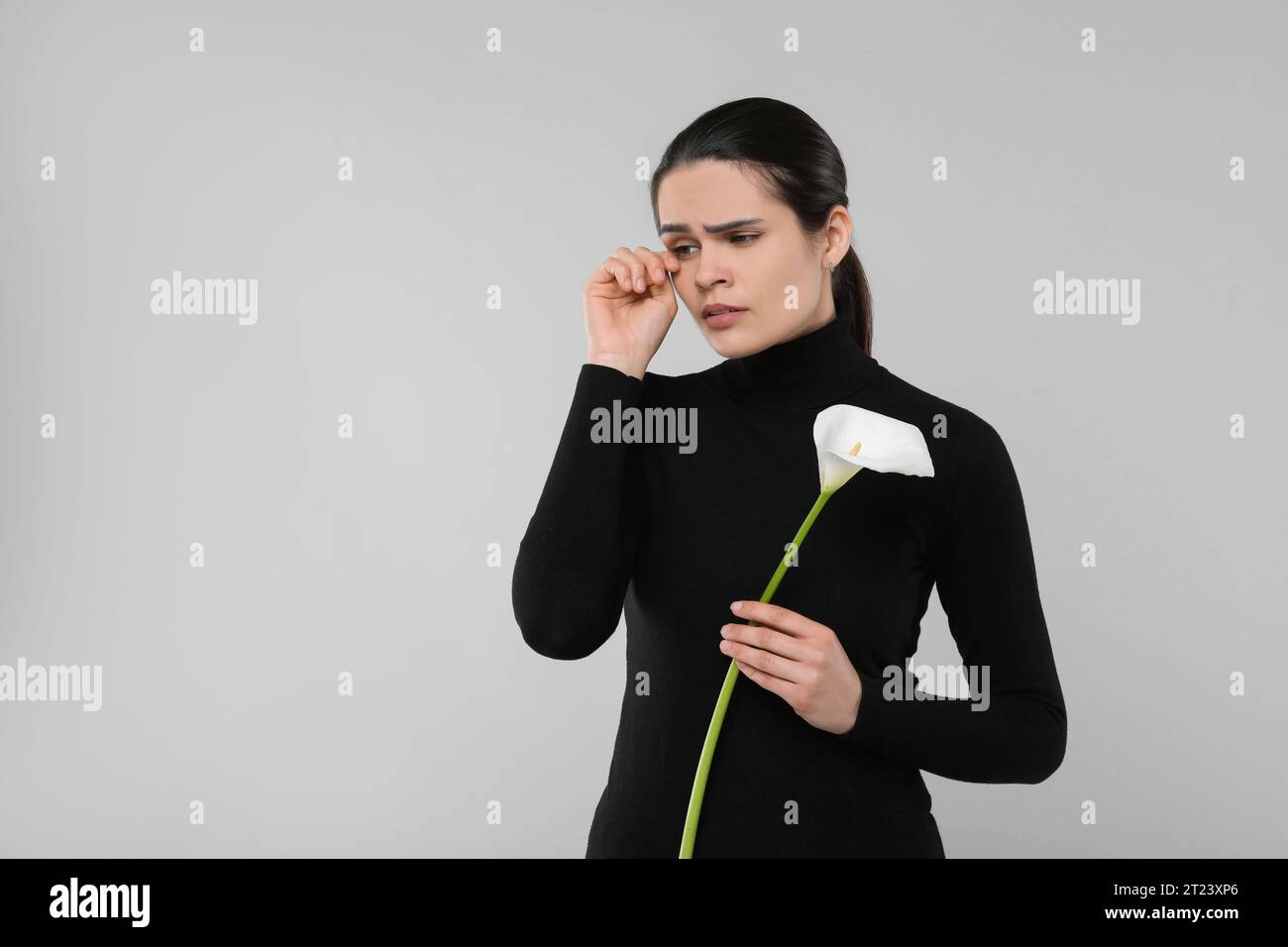 Sad woman with calla lily flower mourning on light grey background ...