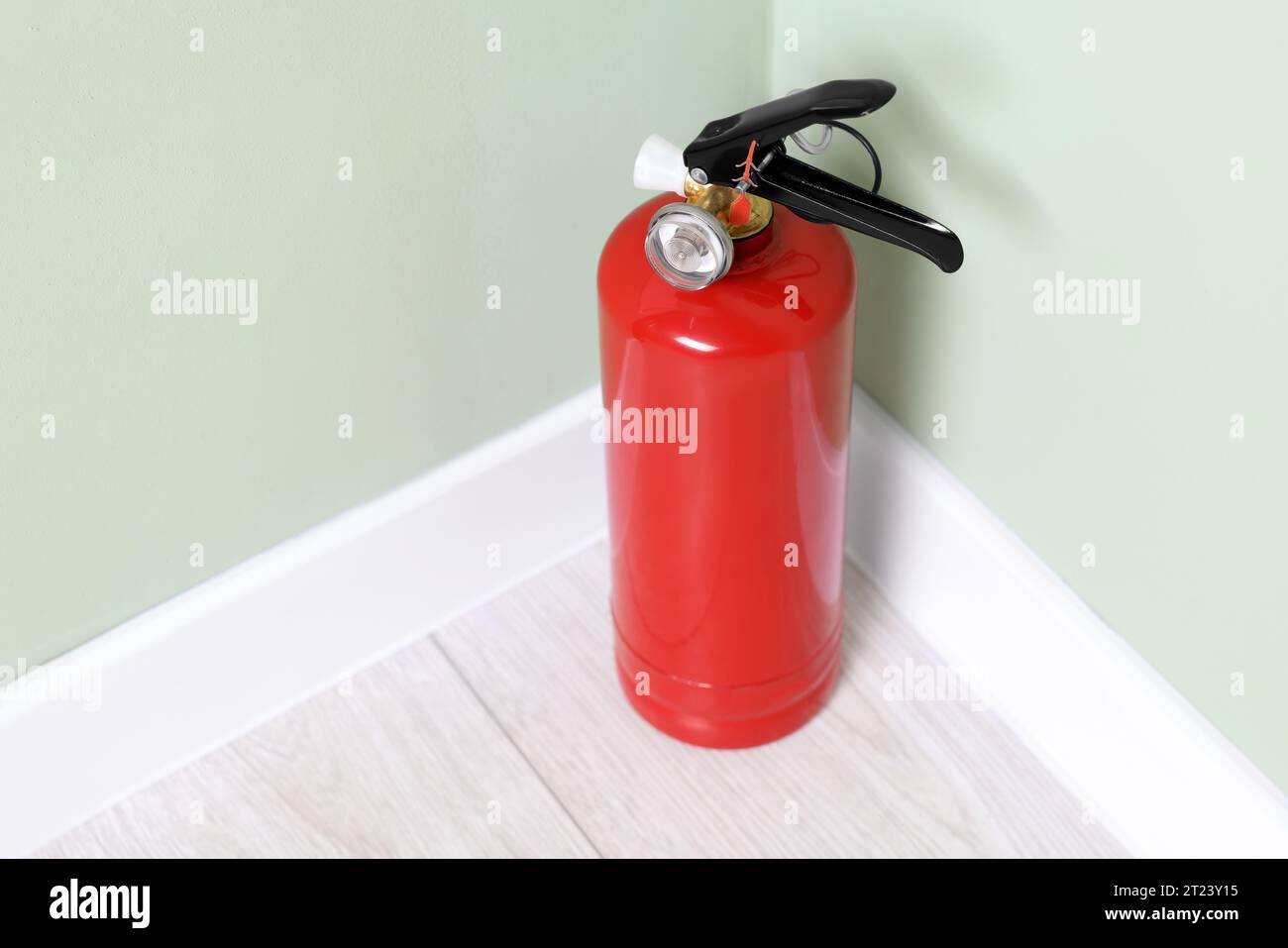 Red fire extinguisher near light green wall Stock Photo - Alamy