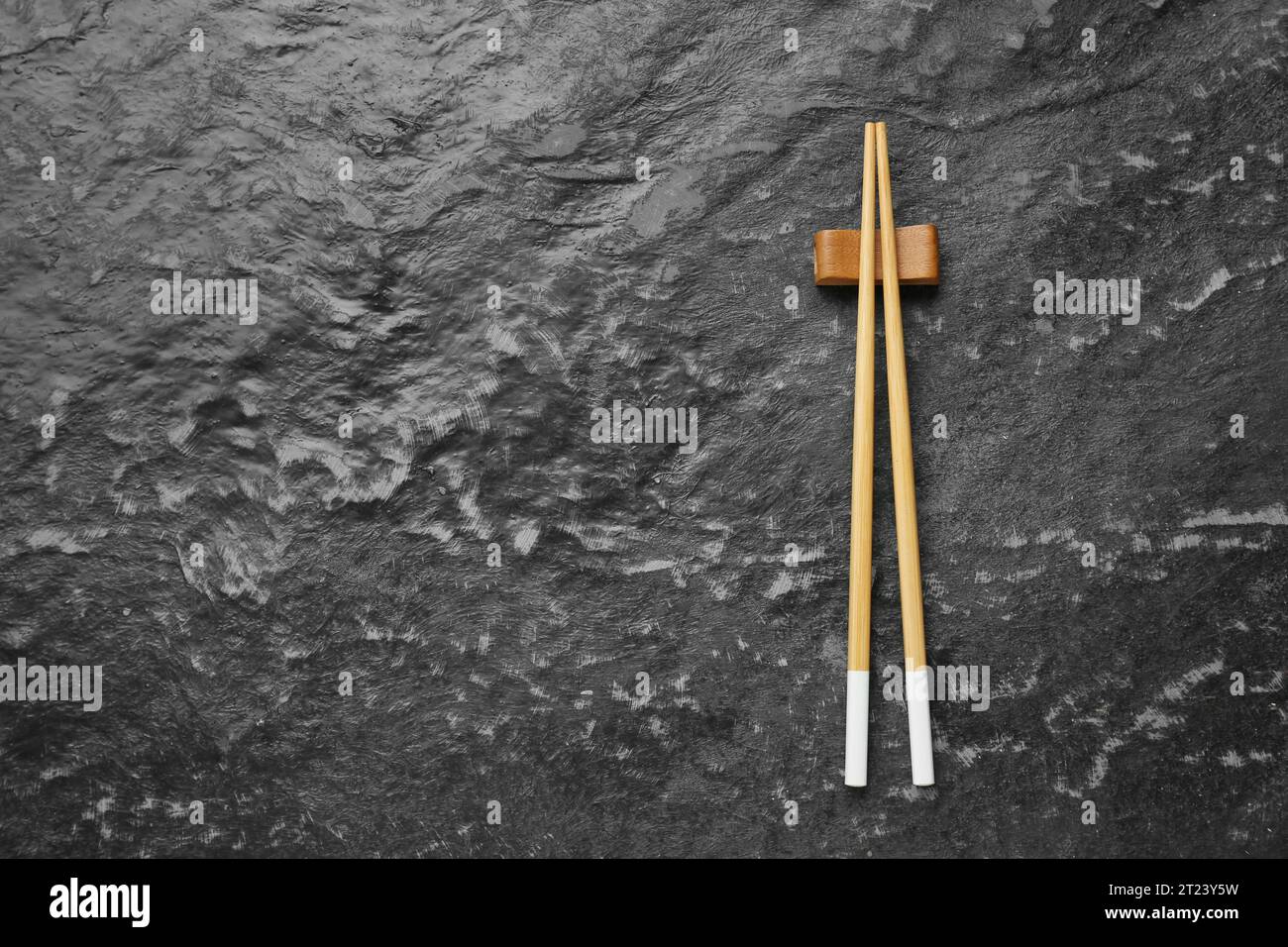 Pair of wooden chopsticks with rest on black textured table, top view ...