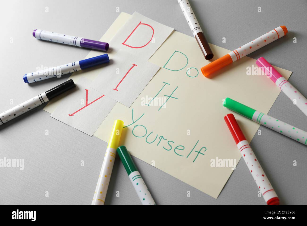 Sheet with written phrase Do It Yourself and colorful markers on grey ...