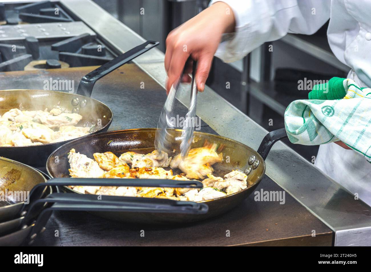 Blurred chefs hands cooking food in pans in a commercial restaurant or ...
