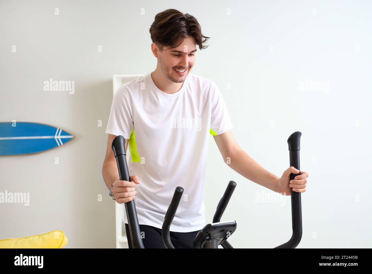 Sporty young man training on elliptical machine at home Stock Photo - Alamy